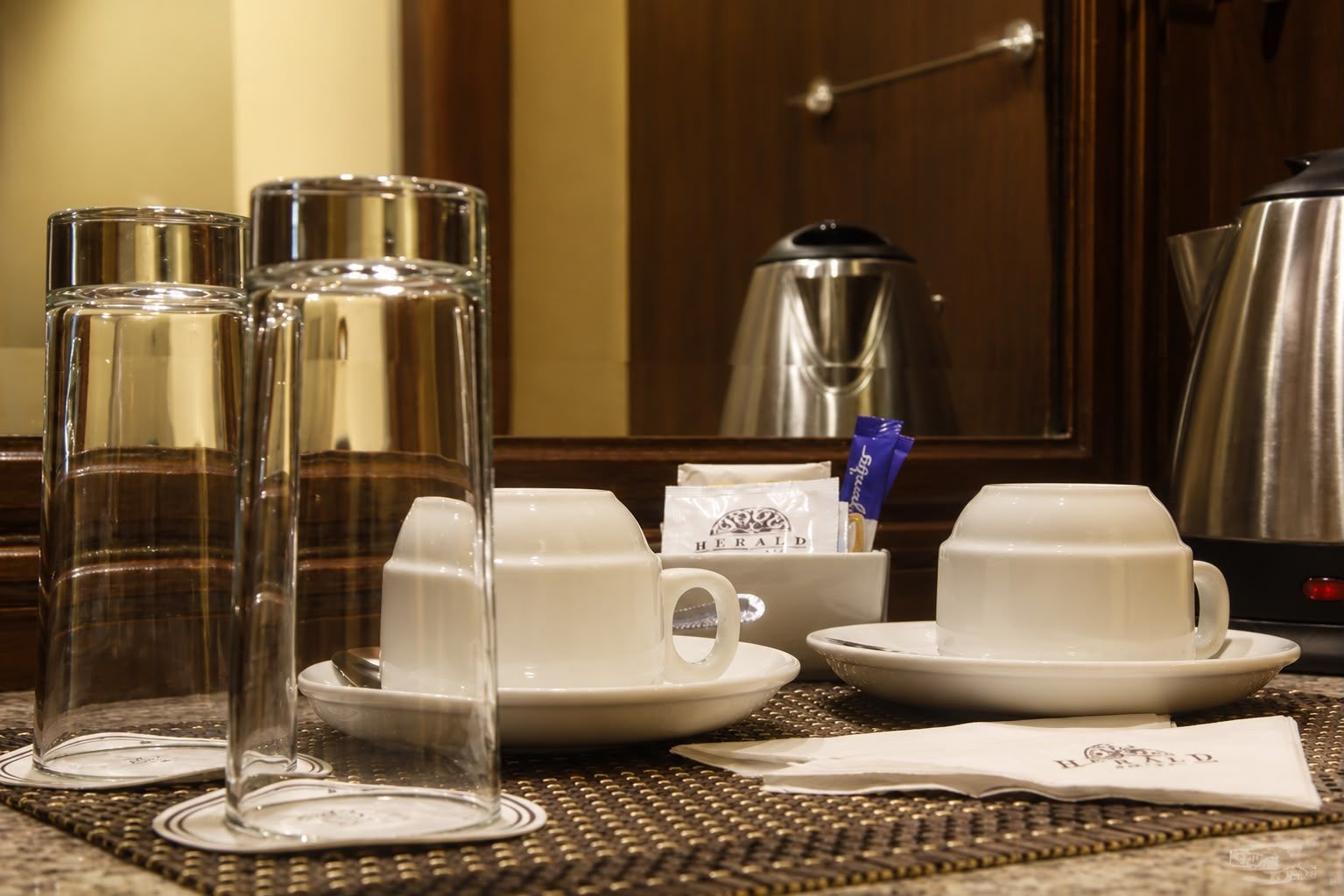 Quarto de hotel com uma cafeteira, duas chávenas e um copo sobre uma mesa.