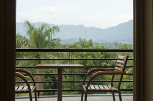 Varanda com mesa e duas cadeiras, dando vista para uma paisagem exuberante com palmeiras e montanhas ao longe.
