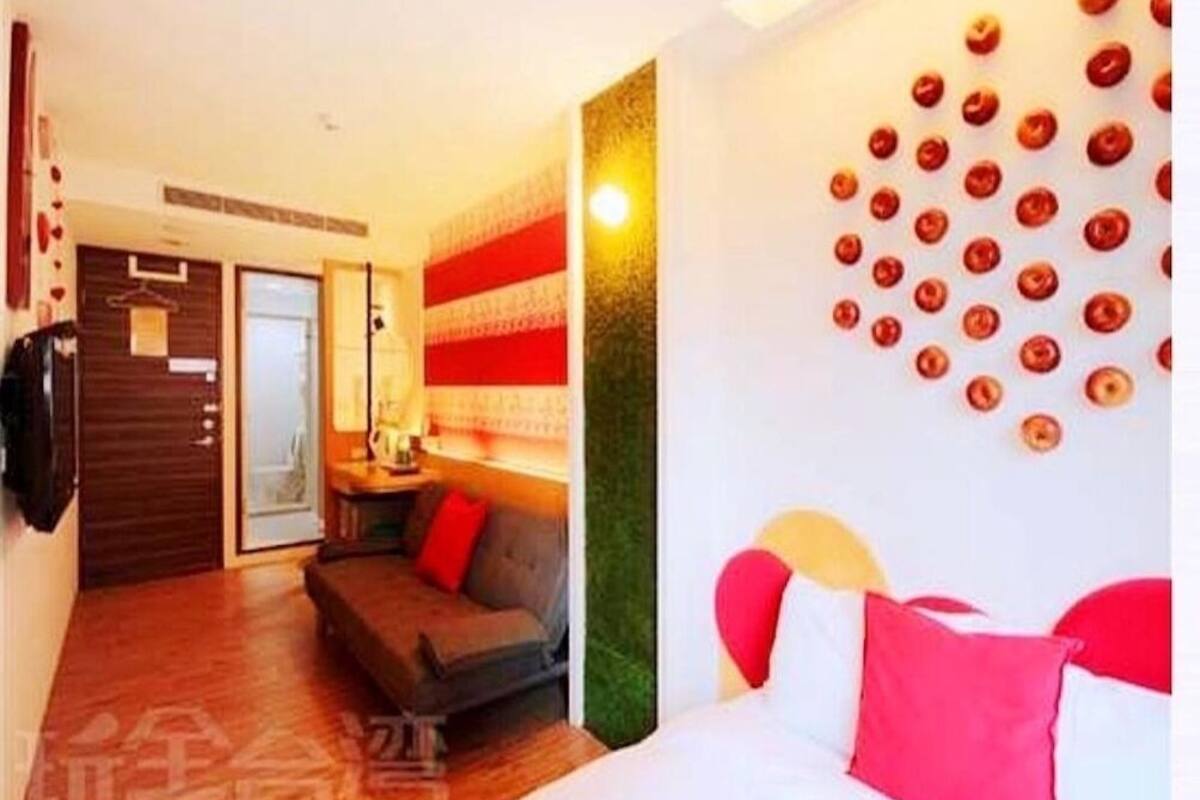Quarto de hotel com cama, sofá, parede com decorações circulares e porta para outro cômodo.