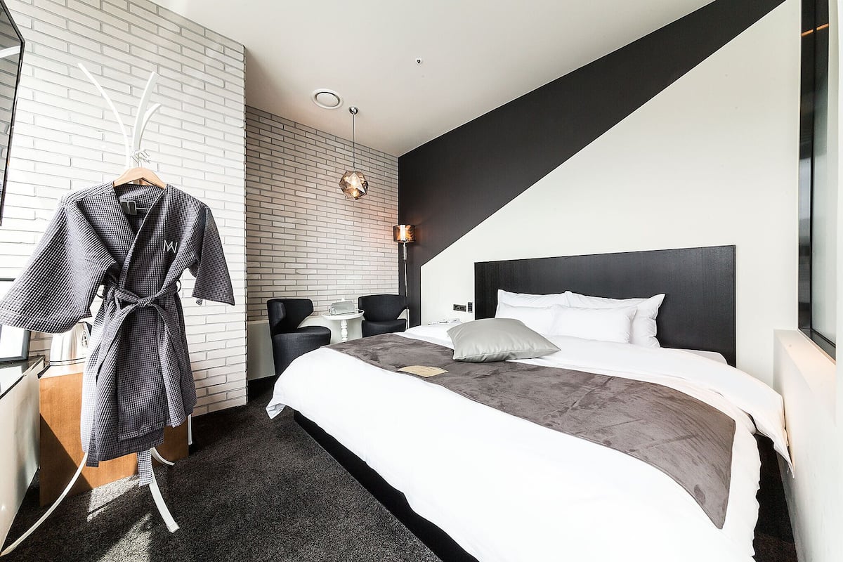 Quarto de hotel moderno com uma cama grande, um roupão pendurado em um porta-roupões, uma escrivaninha e uma cadeira.