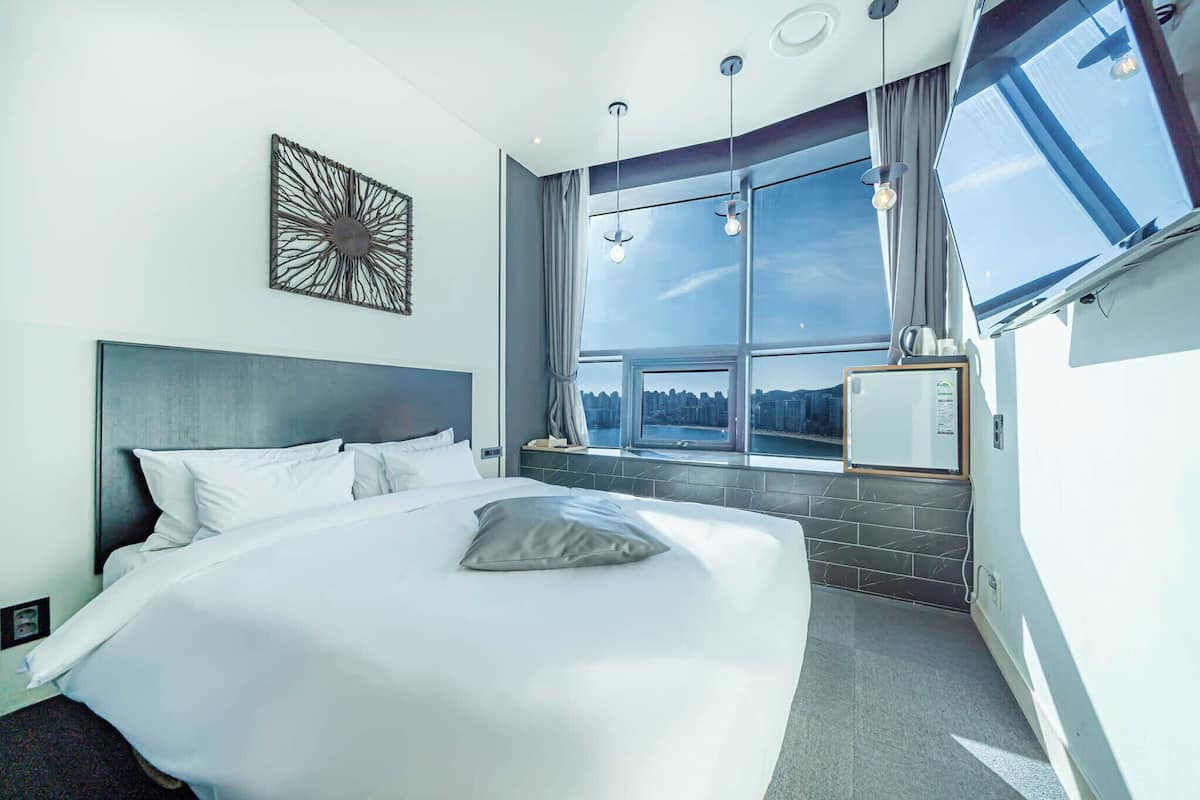Quarto de hotel moderno com uma cama grande, vista da cidade e uma janela ampla.
