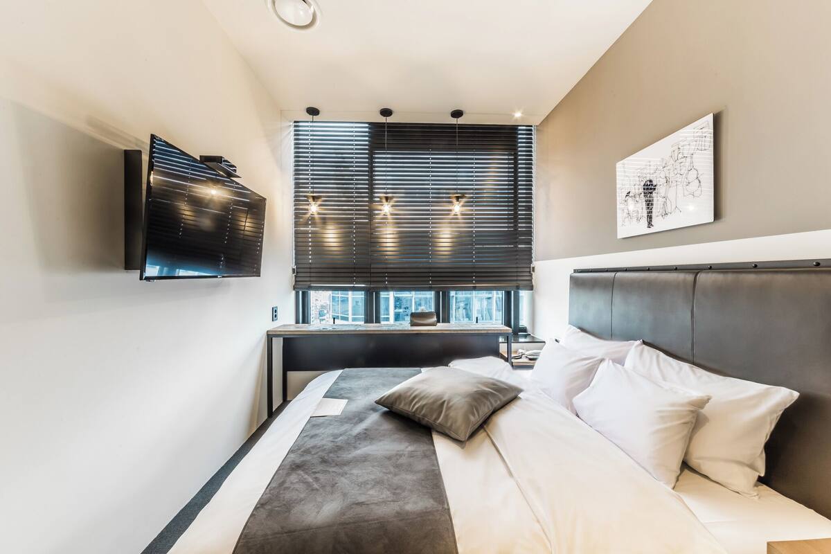 Quarto moderno com cama, televisão de tela plana, escrivaninha e janela com persianas.
