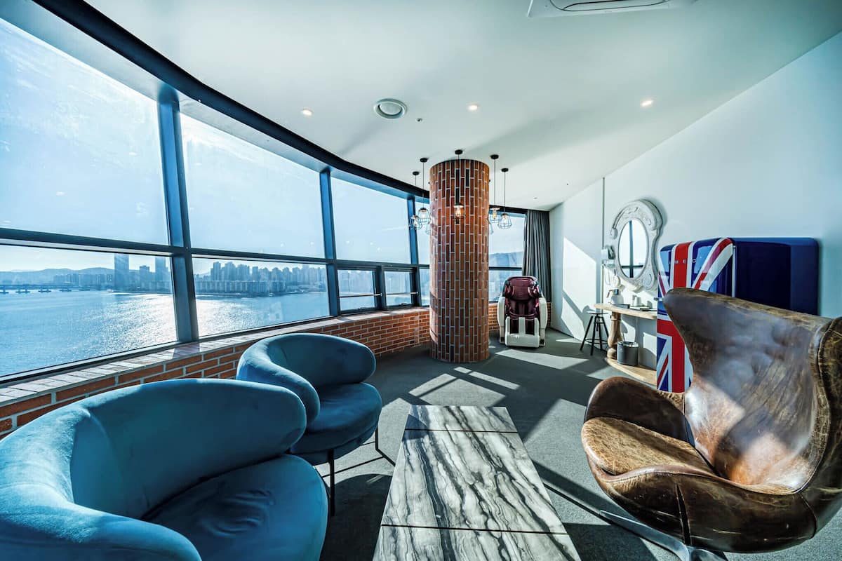 Quarto moderno com grandes janelas, um pilar de tijolos e vista para o horizonte urbano.