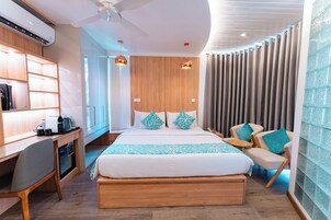 Quarto de hotel moderno com escrivaninha de madeira, cama com roupa de cama estampada, área de estar com cadeiras e uma janela grande com cortinas.