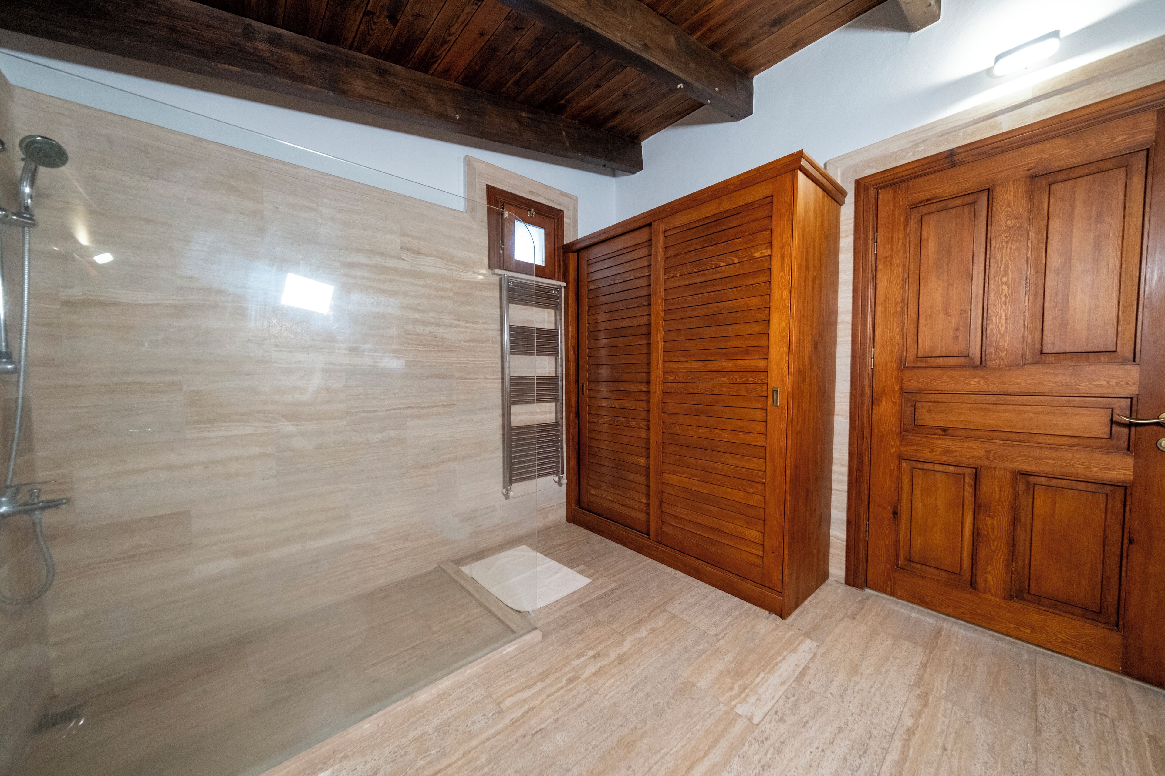 Um banheiro com chuveiro, porta de madeira e piso ladrilhado.