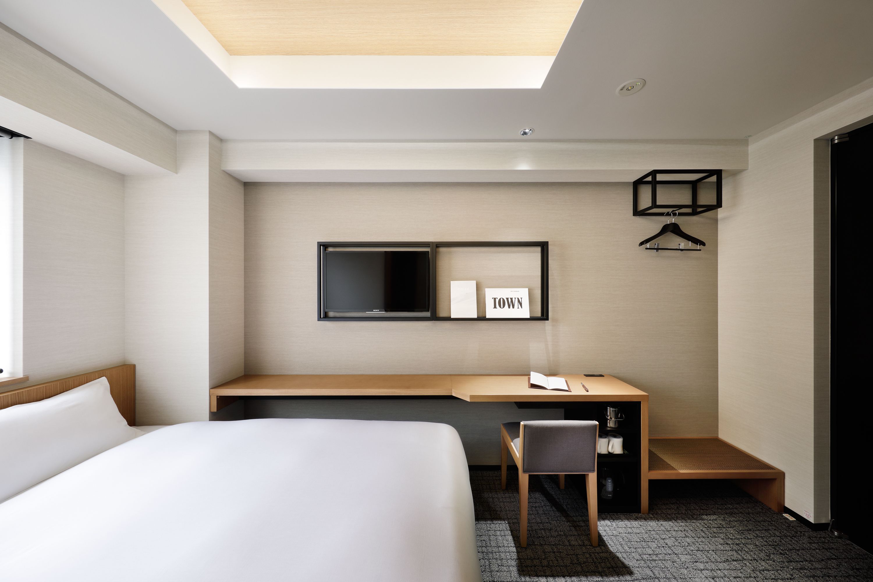 Quarto de hotel moderno com claraboia, uma cama, escrivaninha, cadeira, televisão e cabideiro.