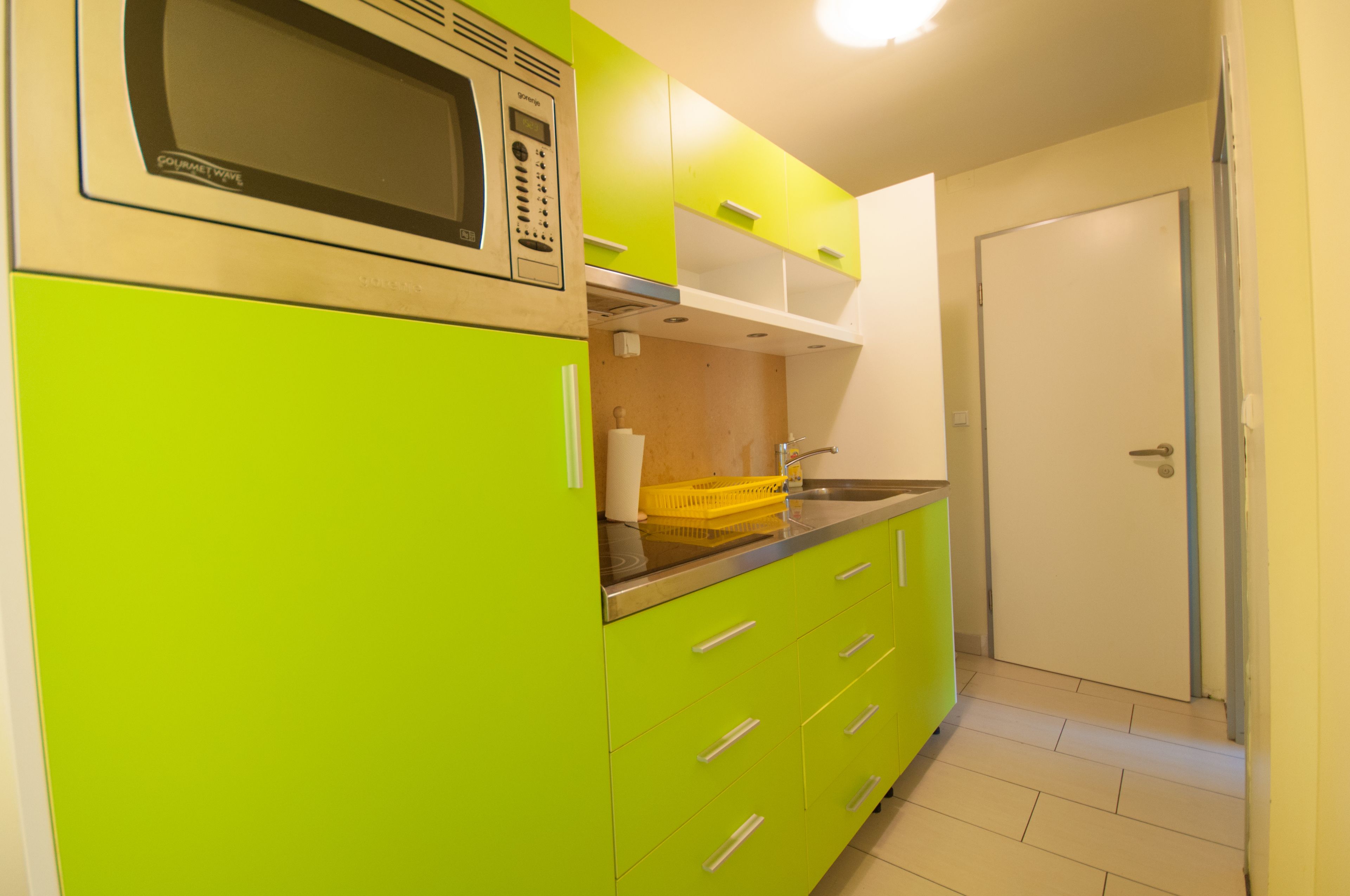 Uma cozinha compacta com micro-ondas, armários verdes e uma porta branca.