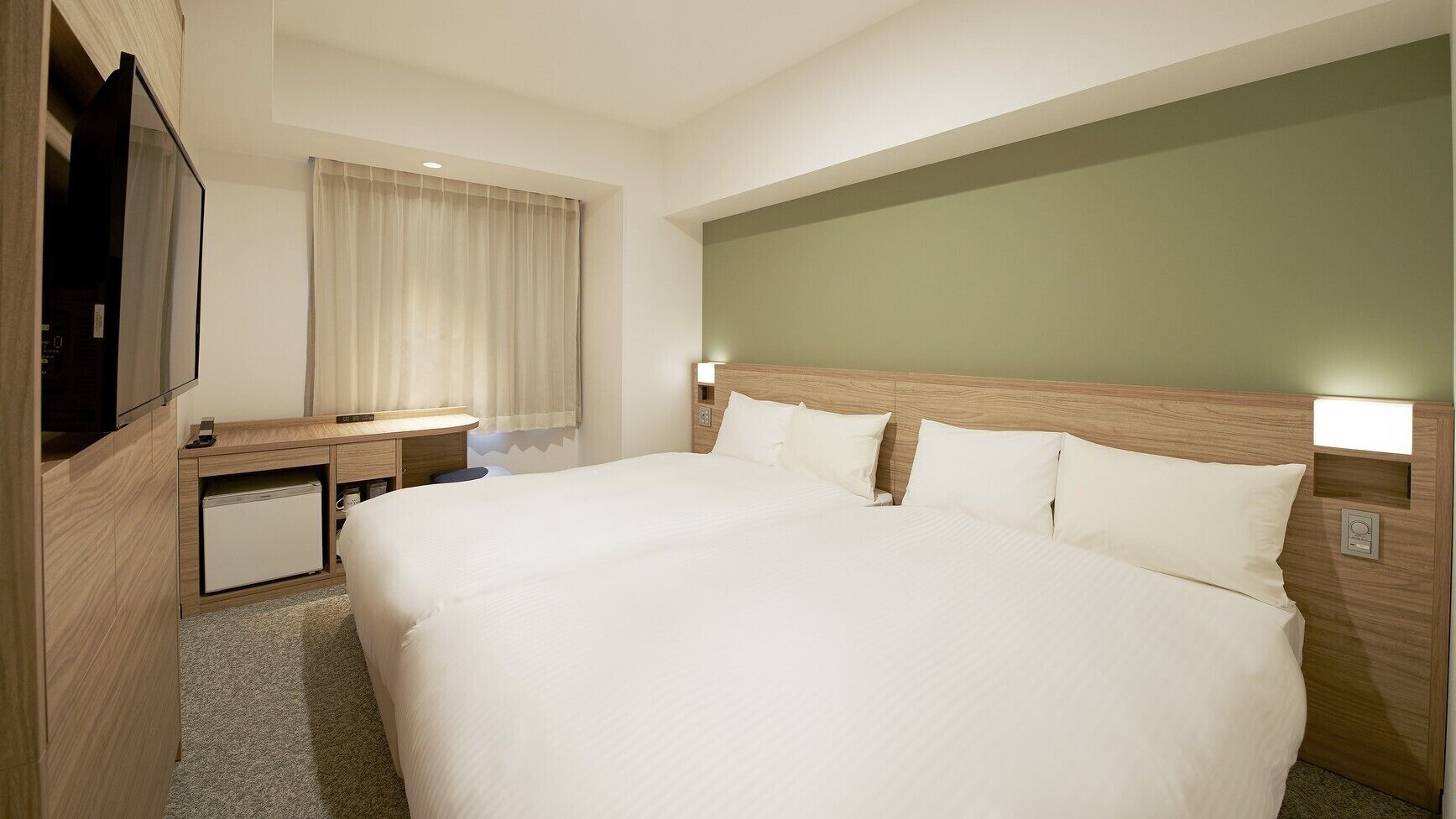 Quarto de hotel com uma cama grande, uma escrivaninha com computador, televisão e mini-frigorífico.