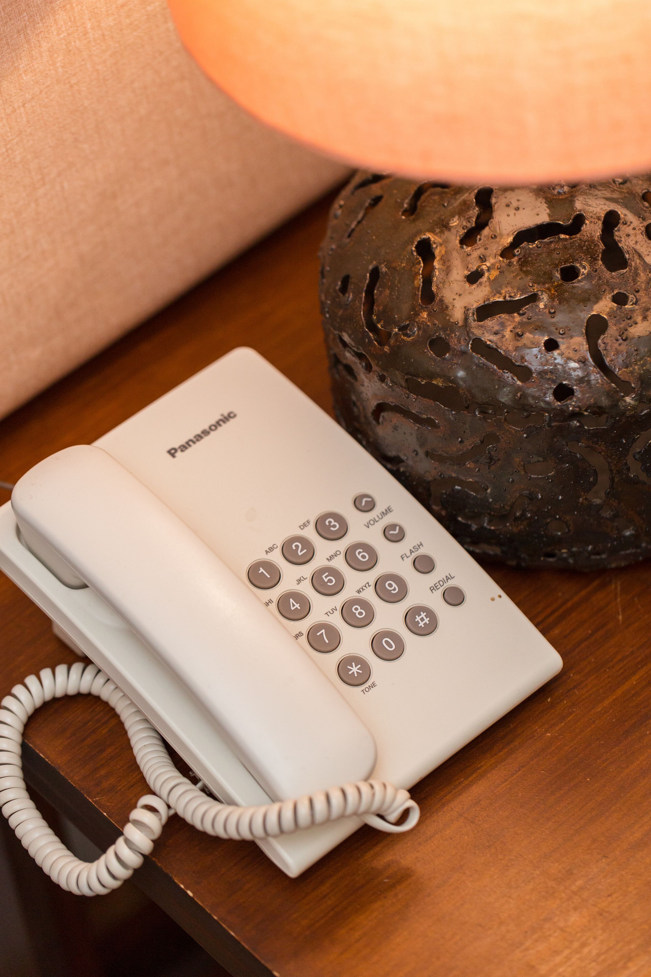 Um telefone Panasonic branco sobre uma superfície de madeira, ao lado de um abajur com textura.