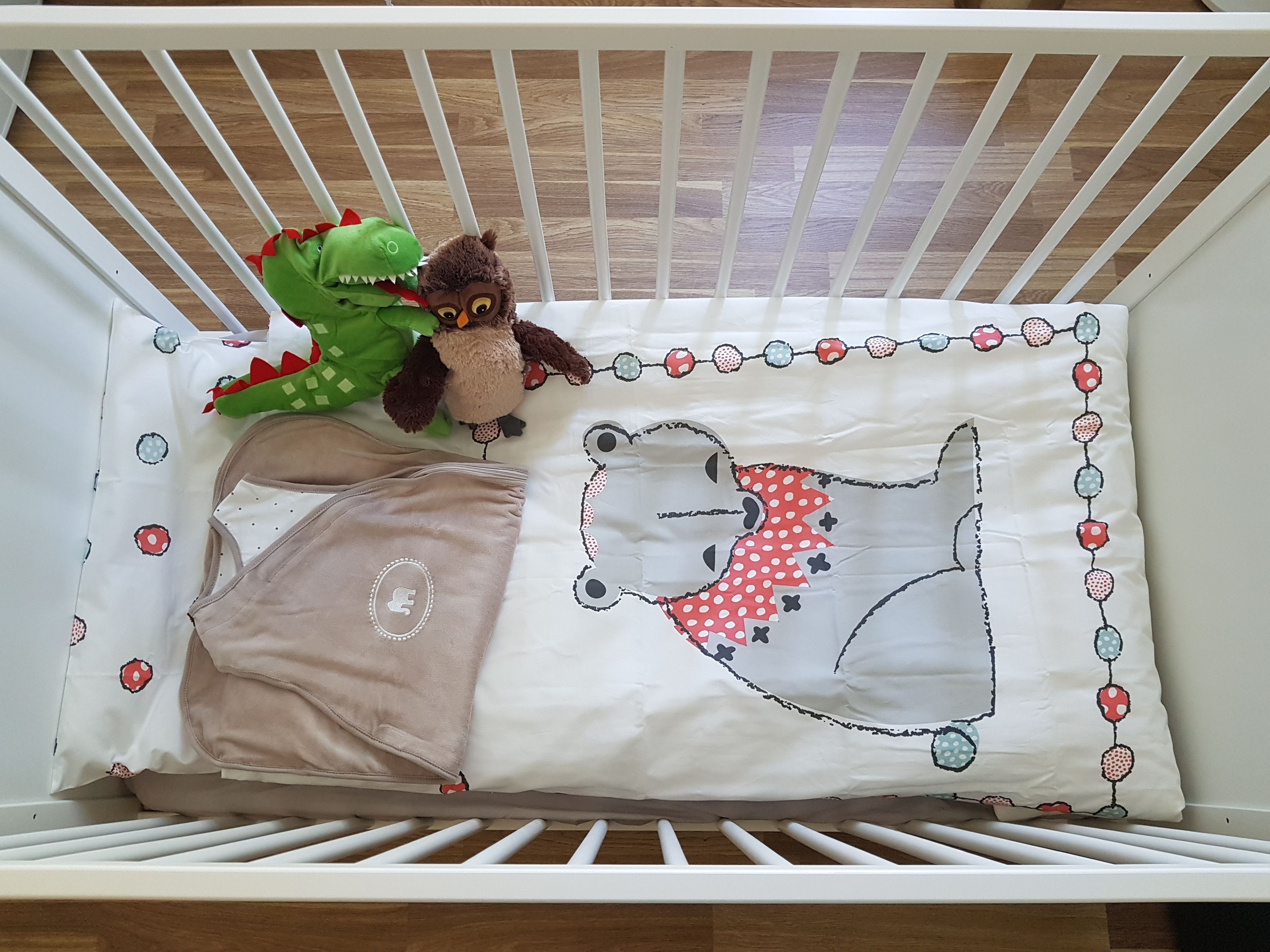 Um berço com estrutura branca, colchão estampado e um brinquedo de pelúcia.