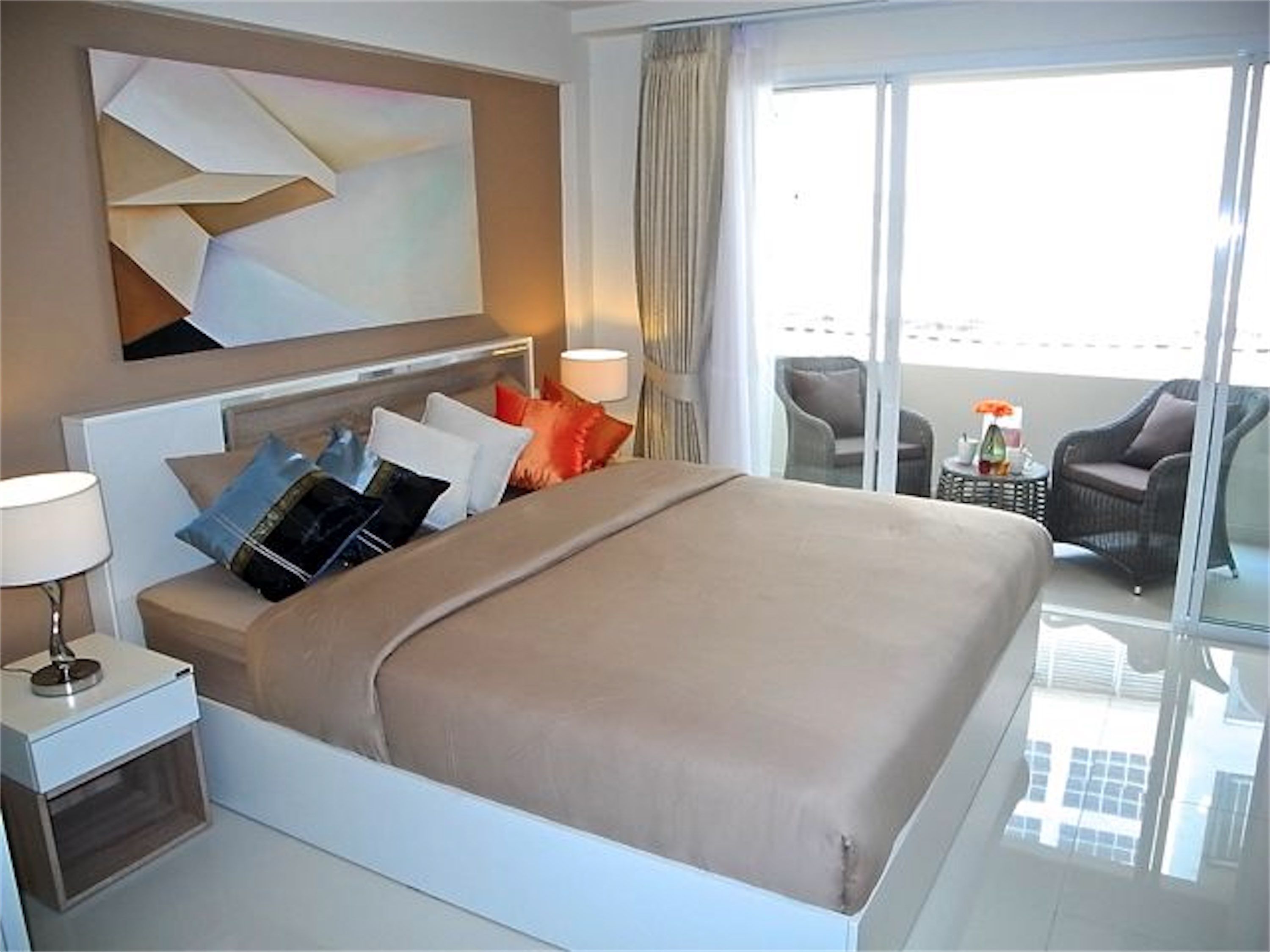 Quarto de hotel moderno com uma cama grande, duas mesas de cabeceira, uma janela ampla com cortinas e uma varanda com cadeiras.