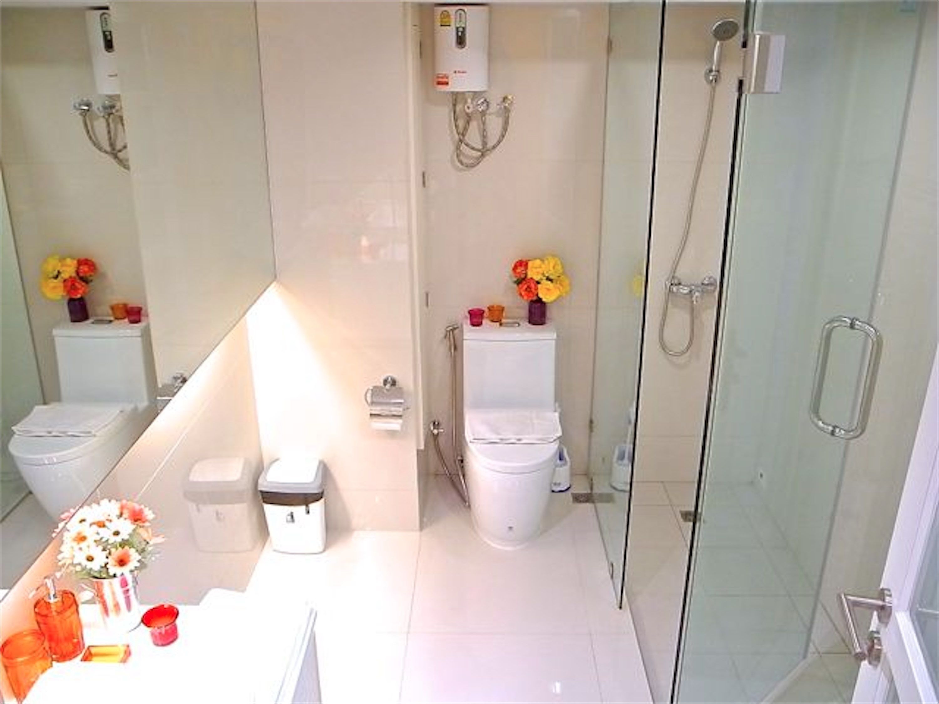 Casa de banho moderna com duas sanitas, chuveiro e área de duche com paredes de vidro.