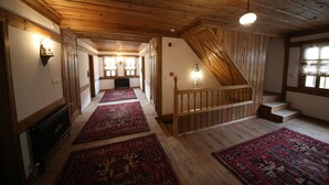 Interior de madeira com escada, tapetes vermelhos e corredor que leva a um quarto com cama.