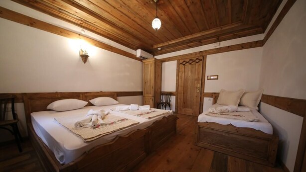 Quarto de madeira com duas camas, uma luminária na parede e uma porta com janela.