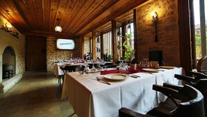 Uma sala de jantar com mesas postas para uma refeição, paredes de pedra, teto de madeira e uma placa com a inscrição "SAFRANBOULU".