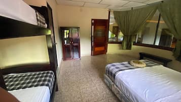 Quarto com beliches, porta de madeira, um banco e janela com cortinas.