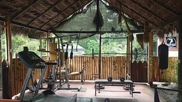 Academia ao ar livre com equipamentos de exercícios, incluindo esteira, banco de musculação e pesos livres.