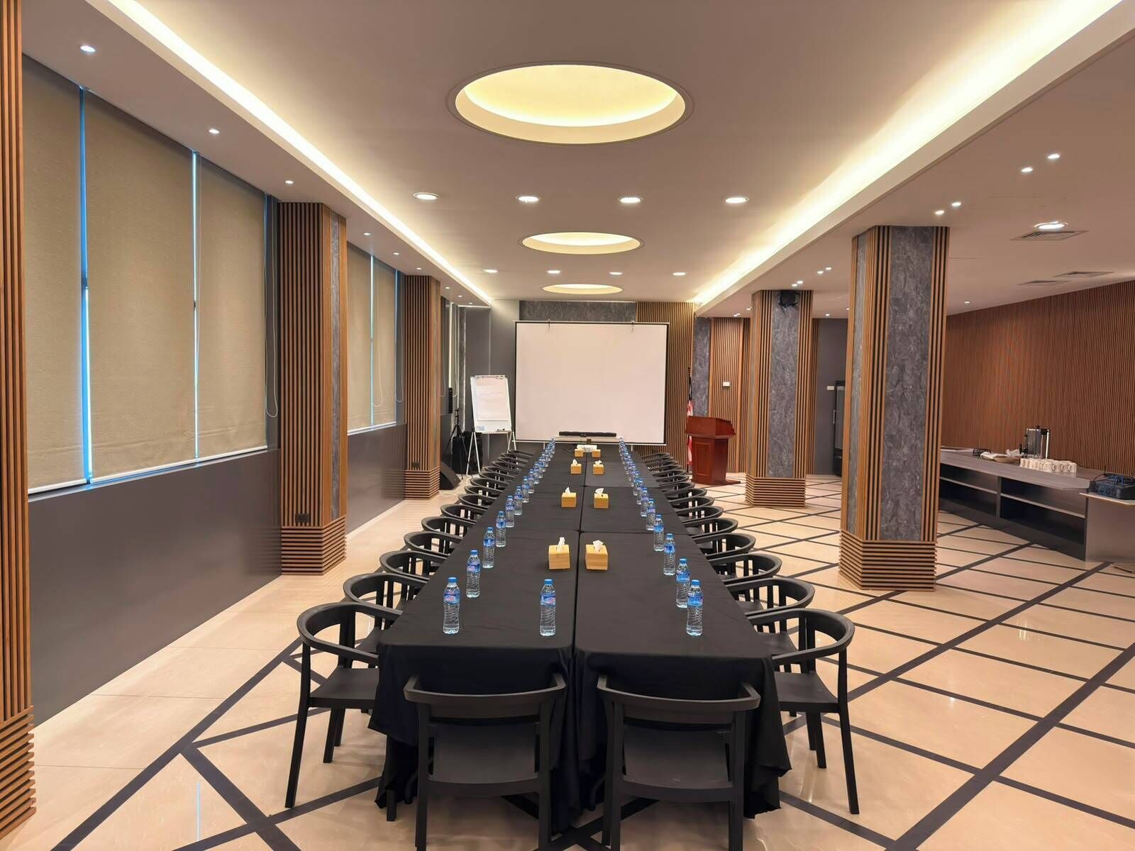 Sala de conferências com uma mesa comprida, cadeiras, um pódio e um quadro branco.