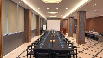 Sala de conferências com uma mesa comprida, cadeiras, um pódio e um quadro branco.