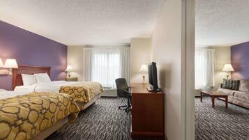 Quarto de hotel com duas camas, uma escrivaninha, uma cadeira, uma televisão e um sofá.
