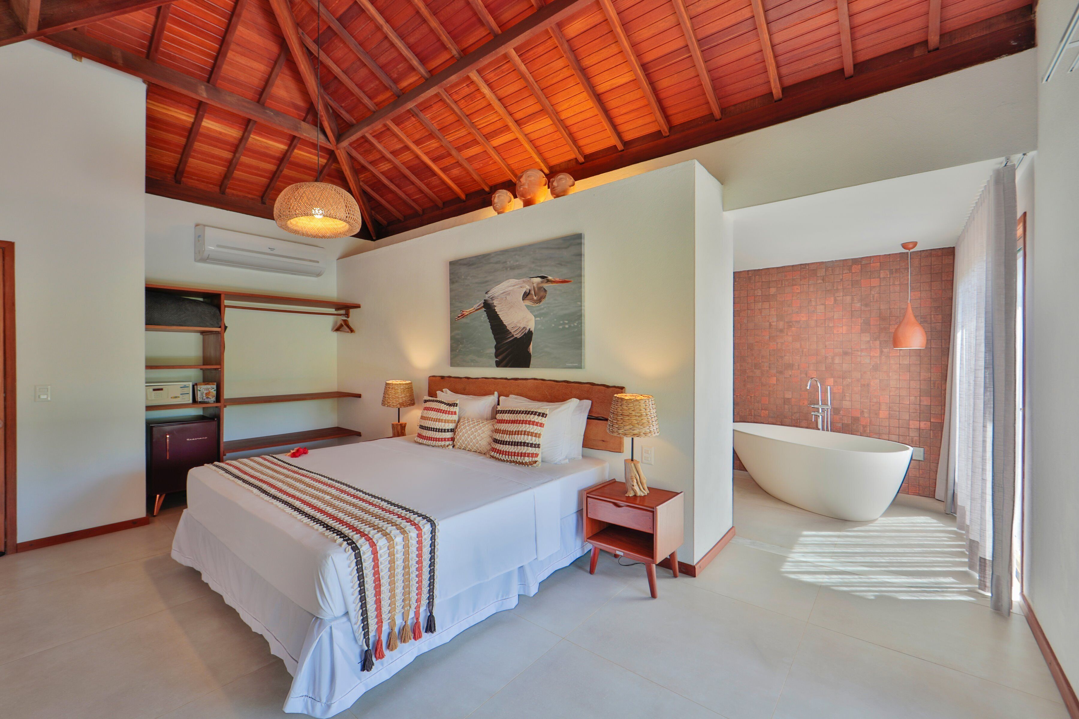 Um quarto espaçoso com uma cama grande, teto de madeira, um quadro, uma mesa de cabeceira com luminárias e um banheiro moderno com banheira.