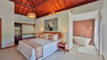 Um quarto espaçoso com uma cama grande, teto de madeira, um quadro, uma mesa de cabeceira com luminárias e um banheiro moderno com banheira.