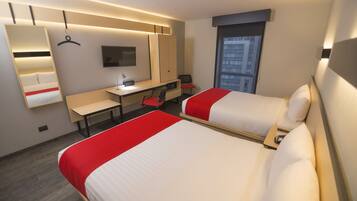 Quarto de hotel com duas camas, uma escrivaninha, uma cadeira, uma televisão e uma janela grande.