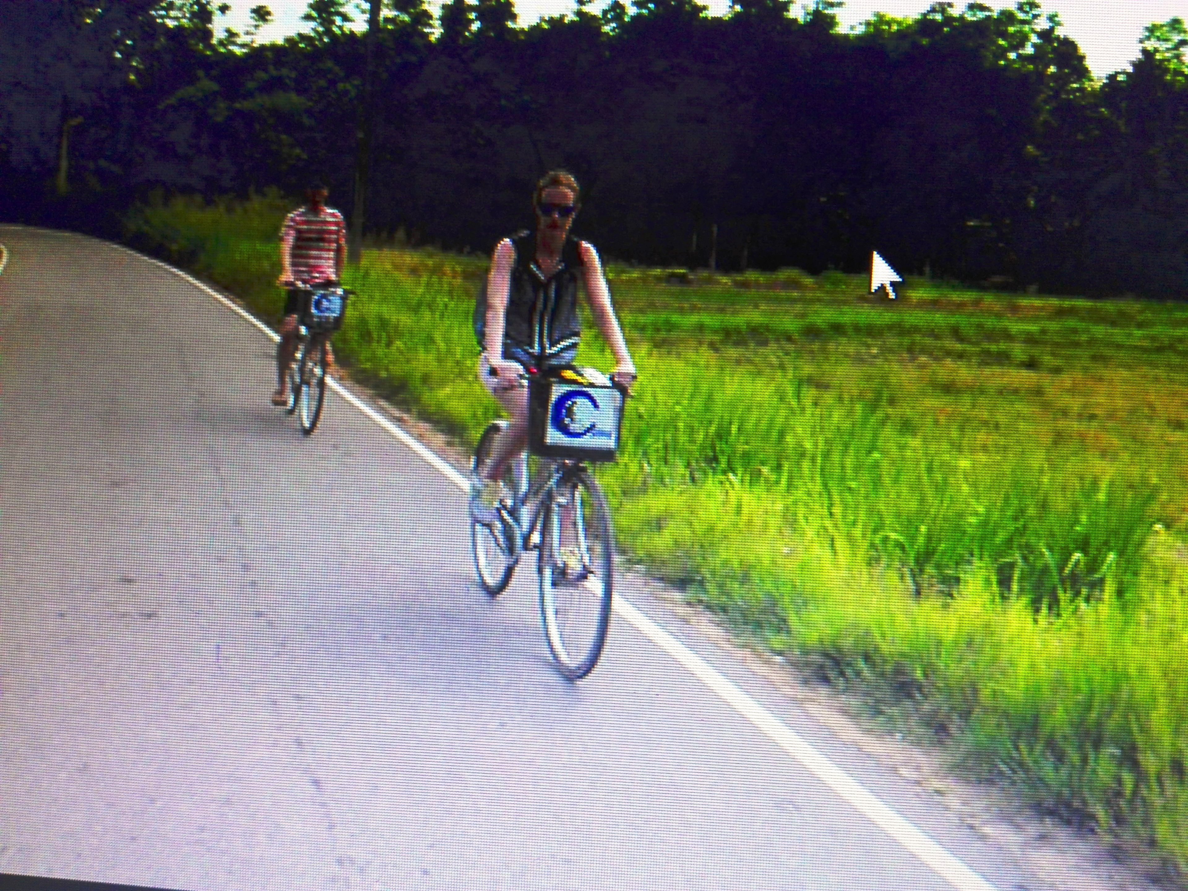 Dois ciclistas em uma estrada com vegetação nas laterais.