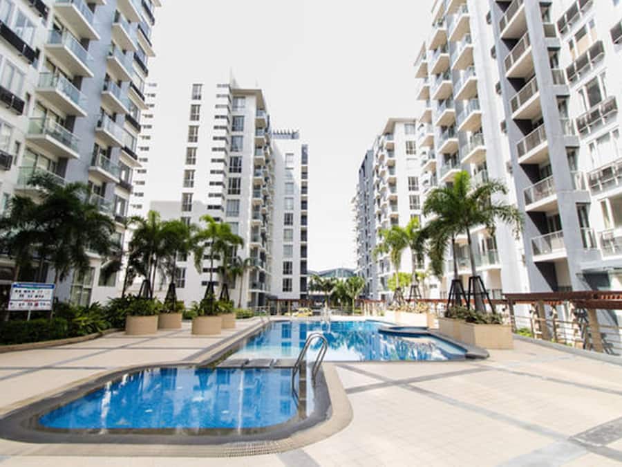 Um edifício residencial moderno com vários andares, piscina central e áreas verdes ao redor.