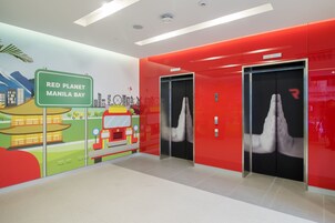 Área moderna de elevadores, com paredes vermelhas e um mural representando uma paisagem urbana e um caminhão de bombeiros.
