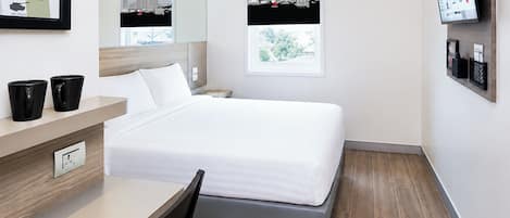 Quarto de hotel com cama, escrivaninha, cadeira, televisão e janela com vista para a cidade.