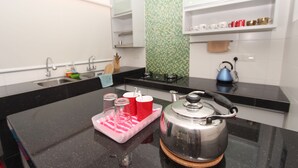 Uma cozinha com bancada preta, chaleira, xícaras vermelhas e bandeja rosa.