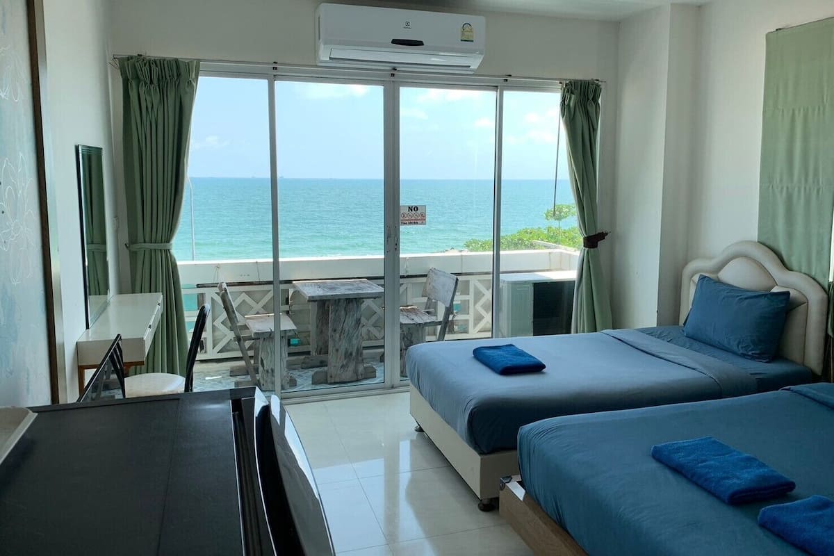 Quarto de hotel com duas camas, televisão e varanda vista para o mar.