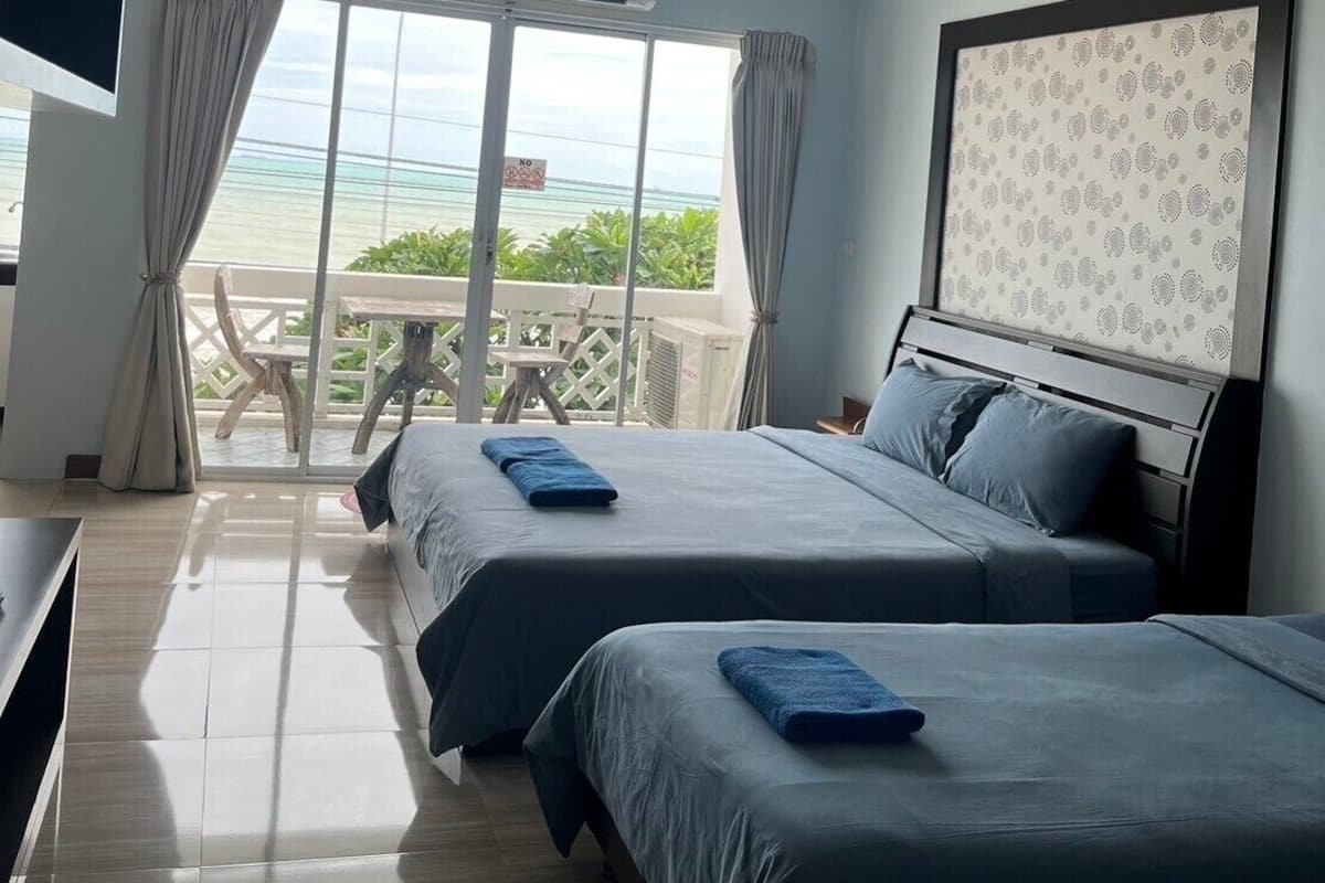 Quarto de hotel com duas camas, televisão e varanda com vista para o oceano.