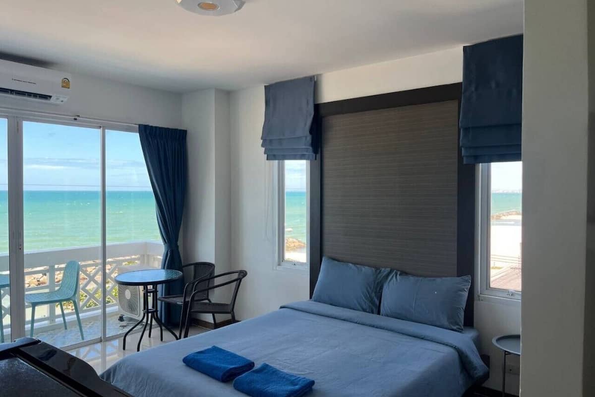 Quarto de hotel com cama, uma pequena mesa, uma cadeira e vista para o oceano.