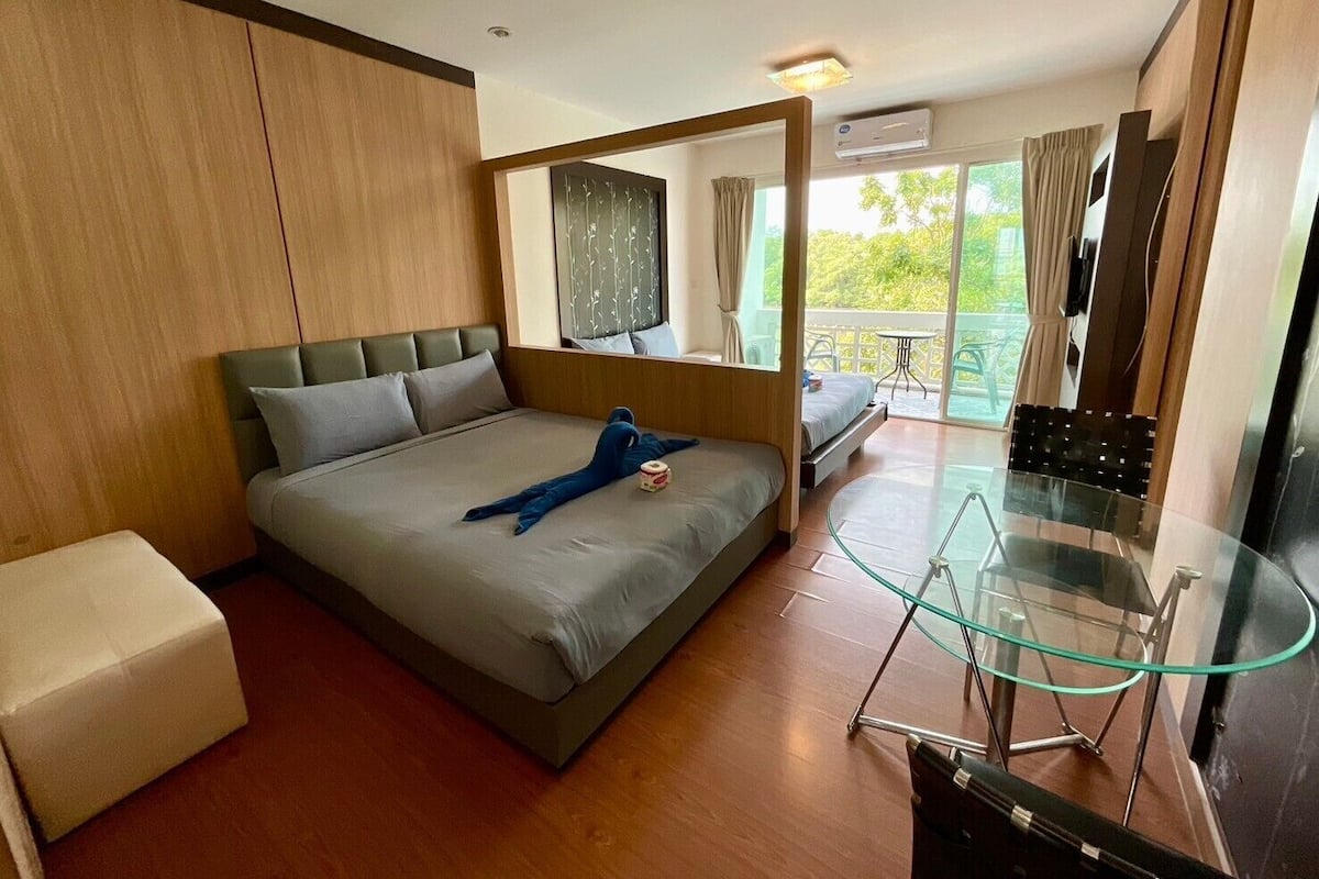 Quarto de hotel moderno com cama, mesa de vidro, televisão e varanda com vista.