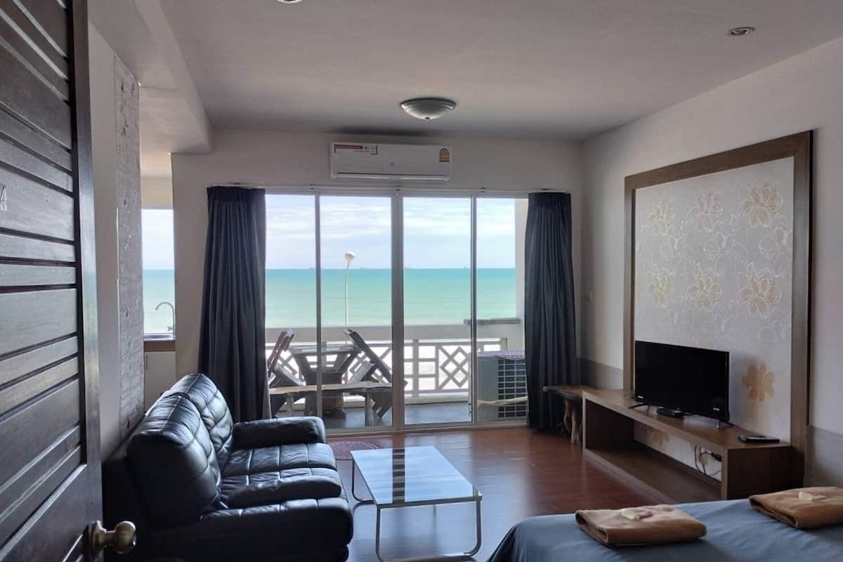 Quarto de hotel com varanda, sofá, televisão e cama.