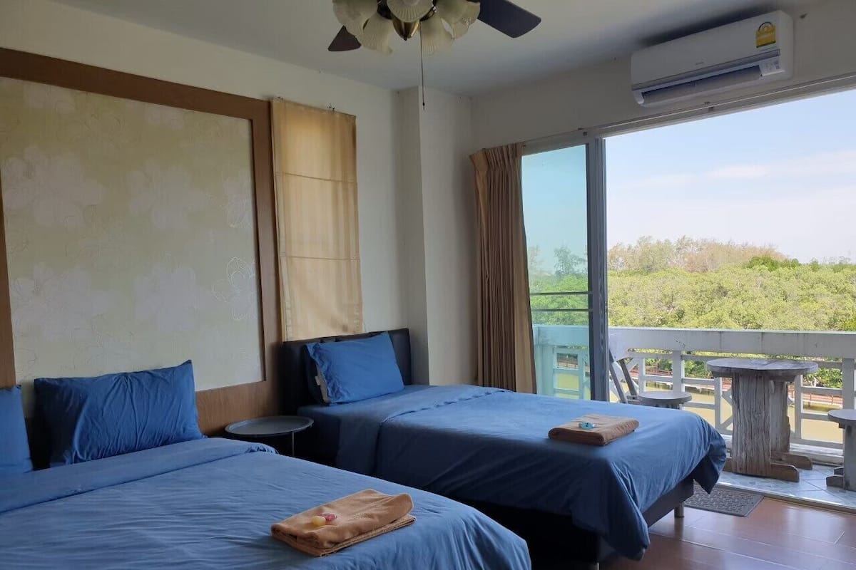 Quarto de hotel com duas camas, ventoinha no teto, ar condicionado e varanda com mesa e cadeiras.