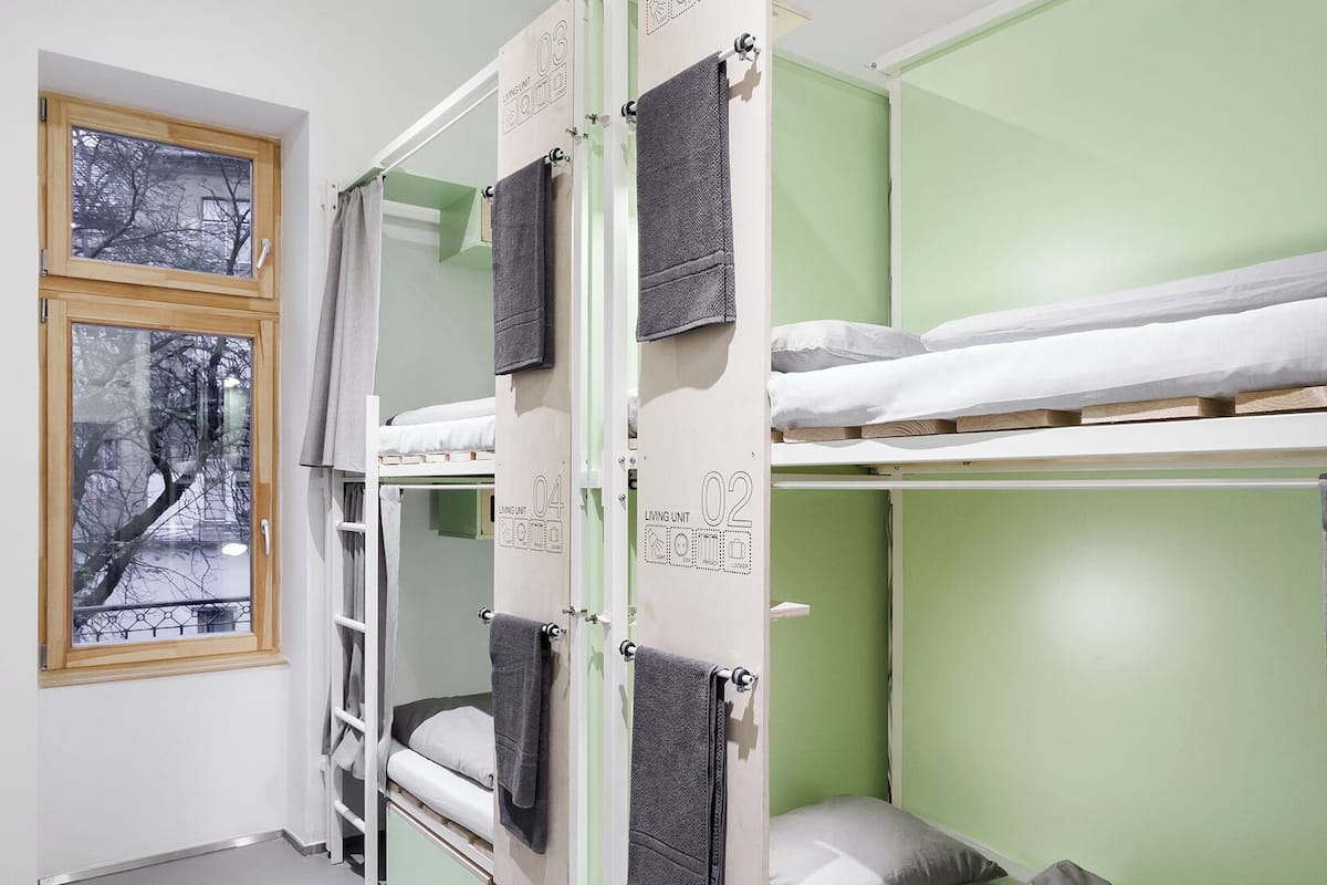 Um quarto de dormitório com beliches, uma janela com vista para árvores e uma porta com uma toalha pendurada.