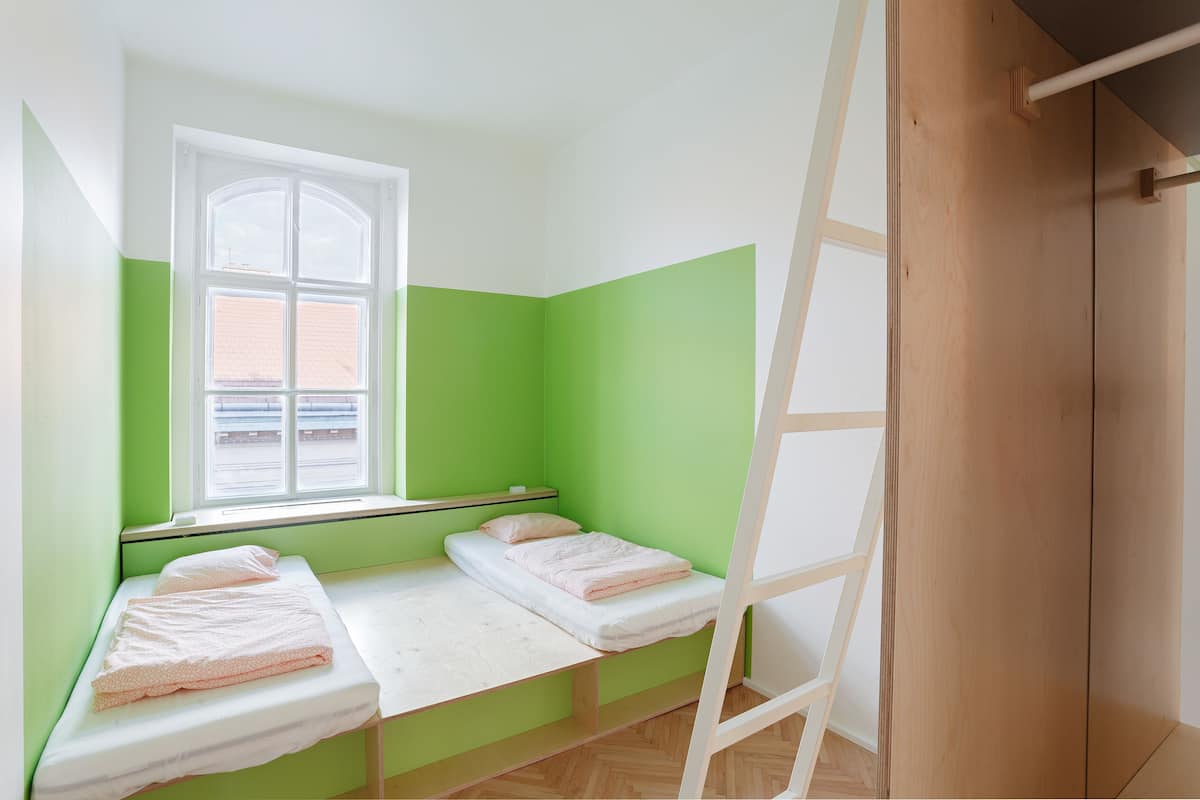 Quarto com duas camas, uma janela e uma escada de madeira.