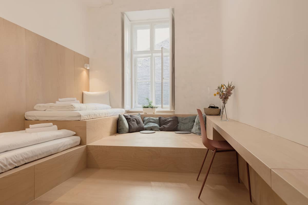 Quarto moderno e compacto com cama, escrivaninha e janela.