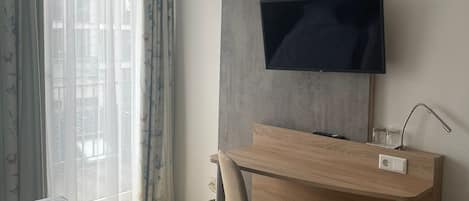 Quarto de hotel com duas camas, uma escrivaninha de madeira, televisão e janela com cortinas.