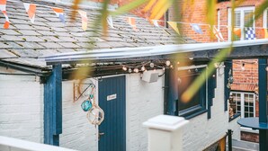 Uma passagem estreita com um edifício branco, uma porta azul com a placa "Private" e uma pequena mesa com uma cadeira.