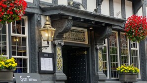 Um pub tradicional com fachada preta e branca, grandes janelas e cestos com flores penduradas.