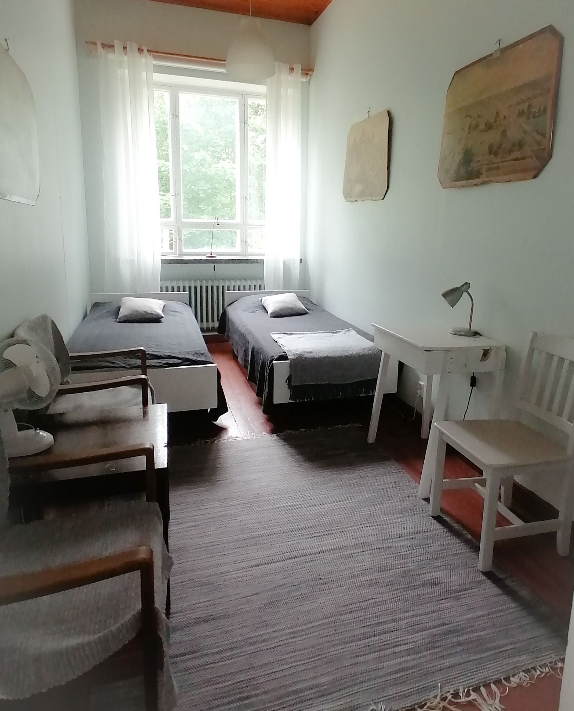 Quarto com duas camas de solteiro, uma mesinha com abajur, uma cadeira e um radiador.