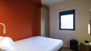Quarto de hotel com cama, janela com vista, mala e abajur.