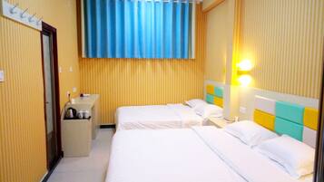 Quarto de hotel com duas camas, uma pequena mesa de cabeceira, um criado-mudo, uma janela com cortinas azuis e um luminário fixado na parede.