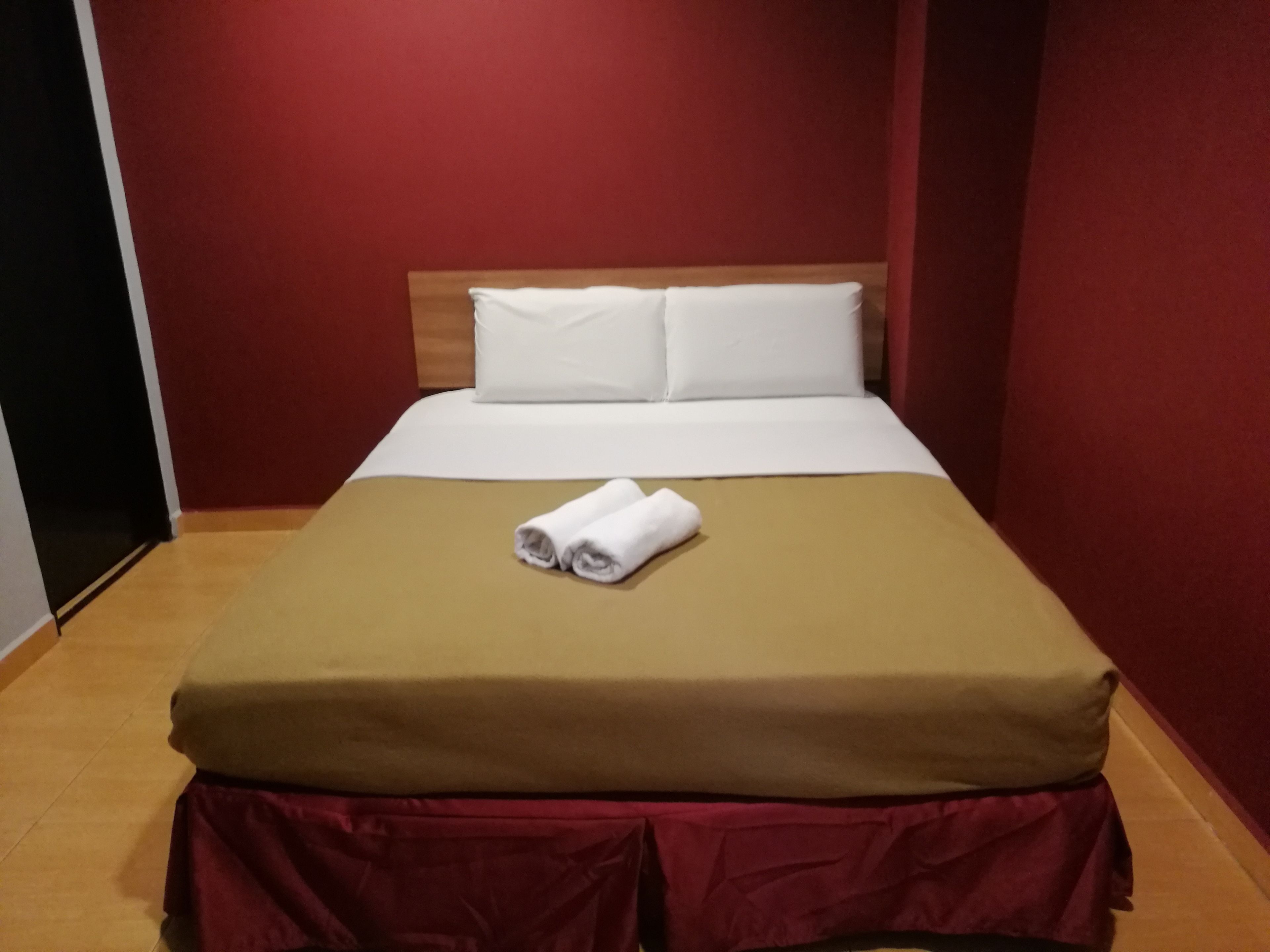 Quarto de hotel com uma cama, almofadas brancas, um edredom marrom e saia para a cama vermelha.