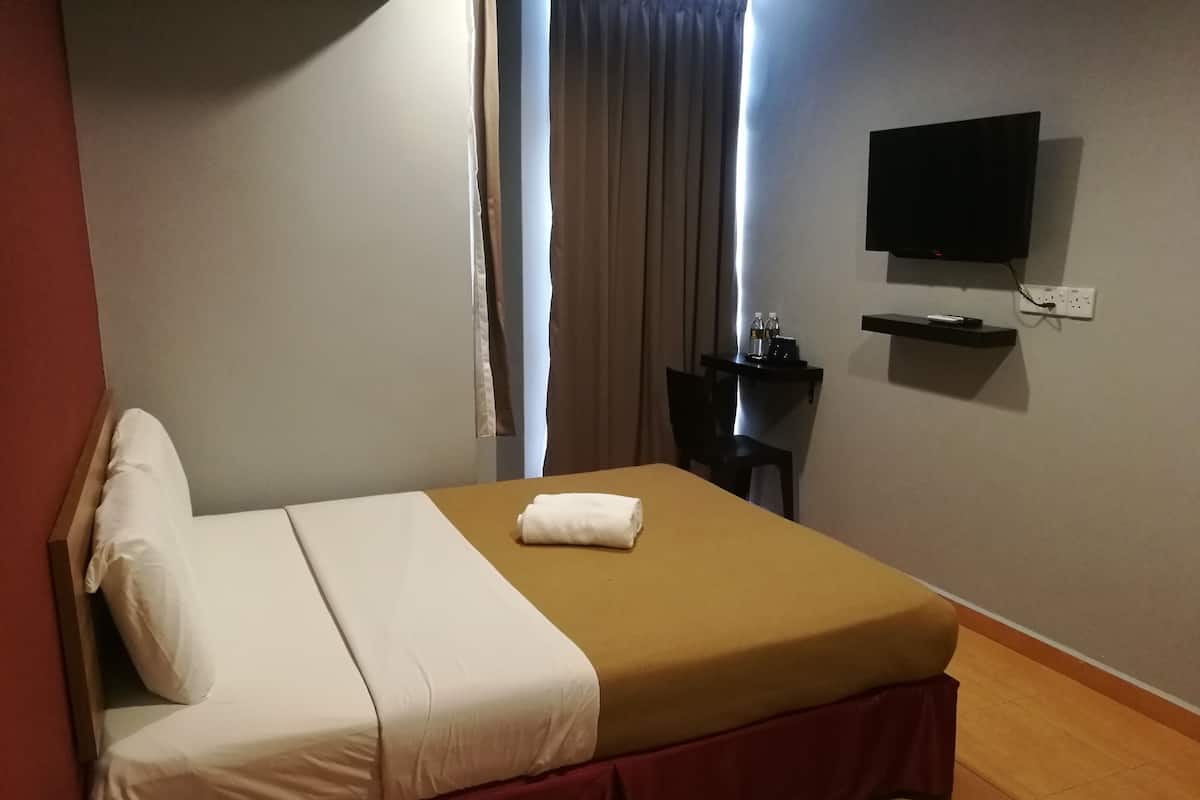 Cama bem arrumada com saia vermelha, uma mesinha com cadeira, TV fixada na parede e um armário com objetos.