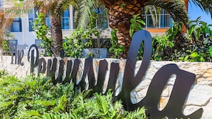 Uma placa grande e chamativa com o texto "The Pointe" em frente a um edifício com parede de pedra e vegetação exuberante.